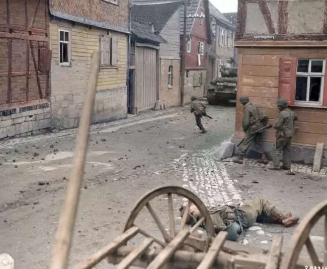 Amerikanische Soldaten, die einen Soldaten verloren haben, versuchen die Straße unter dem Schutz von Sherman-Panzern zu überqueren. Scharfschützenfeuer kommt aus den oberen Stockwerken von Gebäuden, Westdeutschland, ca. 1945